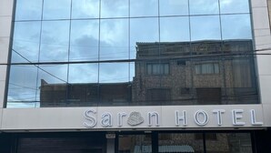 Um edifício moderno com fachada de vidro e o nome "Saron Hotel" em destaque.