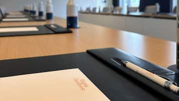 Sala de conferência com uma mesa comprida, garrafas de água, um laptop e uma caneta sobre um tapete preto.