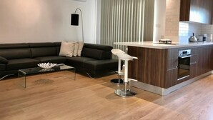 Uma sala de estar moderna com um sofá preto, uma mesa de centro de vidro e um banqueta branca.