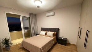 Quarto com cama, mesa de cabeceira, planta em vaso e vista para o exterior.