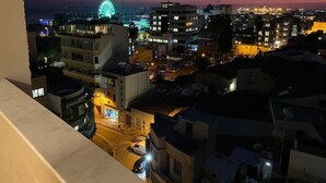 Paisagem urbana noturna com uma roda gigante em destaque ao longe, edifícios iluminados e uma rua movimentada abaixo.