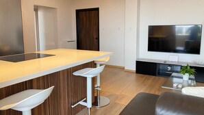 Uma cozinha moderna com área de bar, uma televisão grande, e um espaço de jantar com sofá e planta.