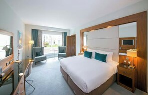 Quarto de hotel com uma cama grande, uma escrivaninha, uma cadeira, uma televisão e uma janela.