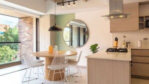 Uma cozinha moderna com uma mesa de jantar redonda, cadeiras brancas e uma janela grande com vista para áreas verdes.
