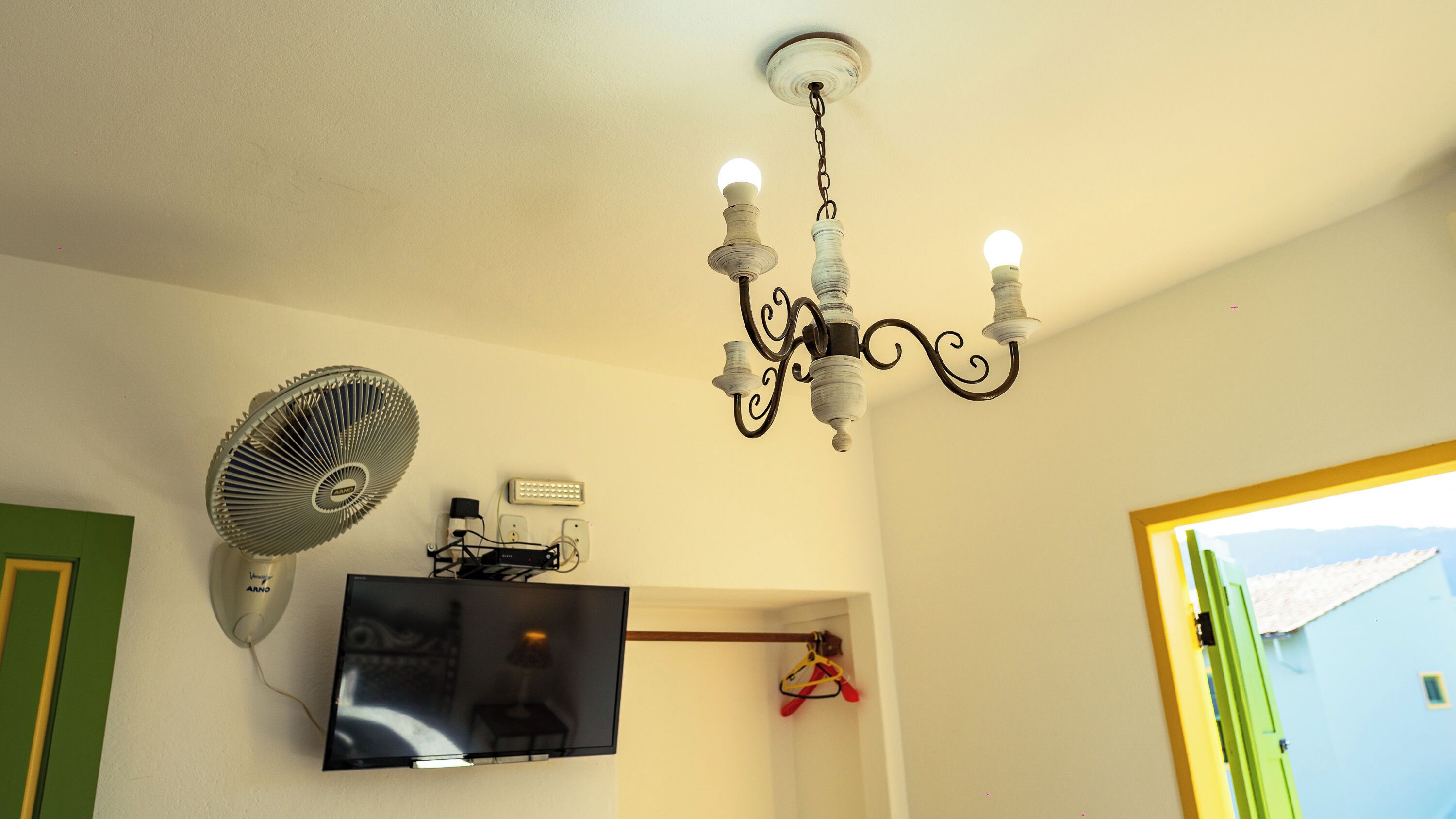 Quarto com lustre, ventoinha na parede e televisão.
