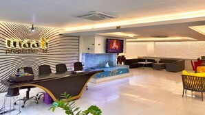 Uma área de recepção com design moderno, incluindo um balcão de atendimento, espaço de espera e uma tela de televisão.