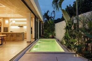 Cozinha moderna com área de bar, piscina e plantas tropicais exuberantes.