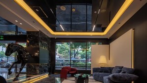 Um lobby moderno com piso de mármore, uma escultura, uma cadeira vermelha, um sofá azul e uma grande janela com vista para o exterior.