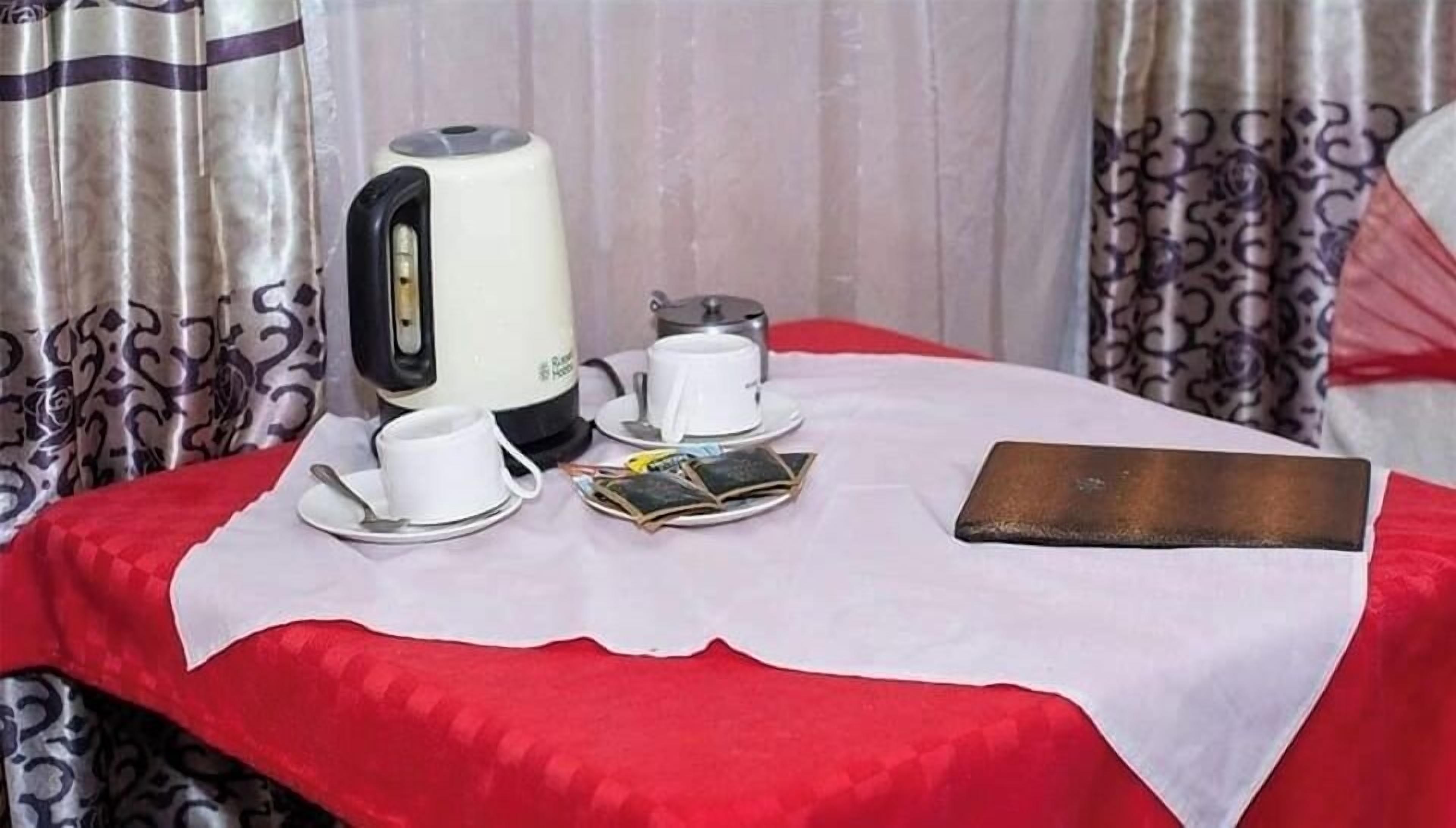 Uma mesa com toalha branca, chaleira, duas chávenas, bandeja de chá e uma carteira.