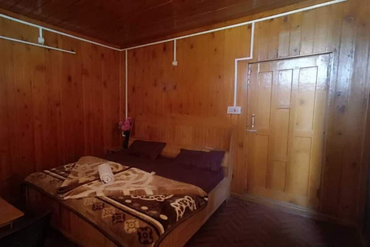 Um quarto com painéis de madeira, uma cama, uma mesinha e uma porta.
