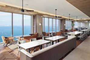 Uma sala de jantar moderna com pé direito alto, janelas amplas e vista para o mar.