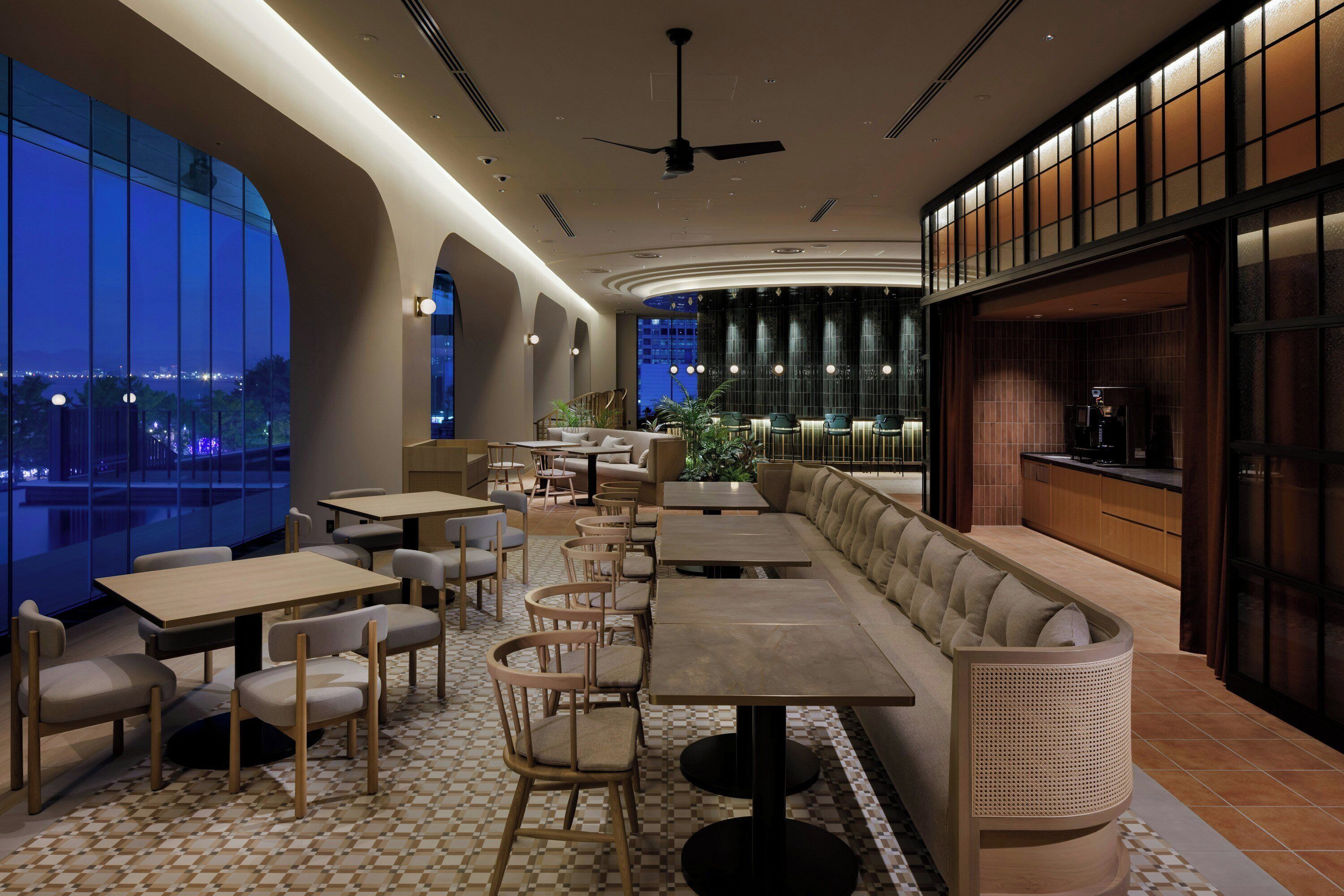 Um restaurante moderno com um balcão comprido, área de estar, janelas amplas e vista para o horizonte da cidade.