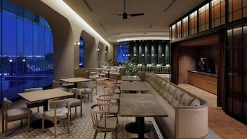 Um restaurante moderno com um balcão comprido, área de estar, janelas amplas e vista para o horizonte da cidade.