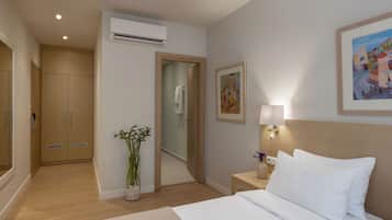 Quarto de hotel com cama, mesa de cabeceira, luminária, obras de arte e banheiro com chuveiro e vaso sanitário.