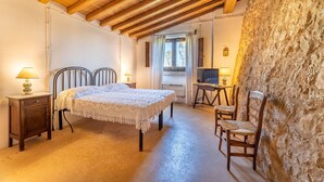 Quarto com teto de madeira, cama com cobertura de renda, escrivaninha com abajur e parede de pedra.