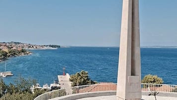Um monumento alto com uma passarela curva em frente, com vista para uma cidade costeira e o mar.