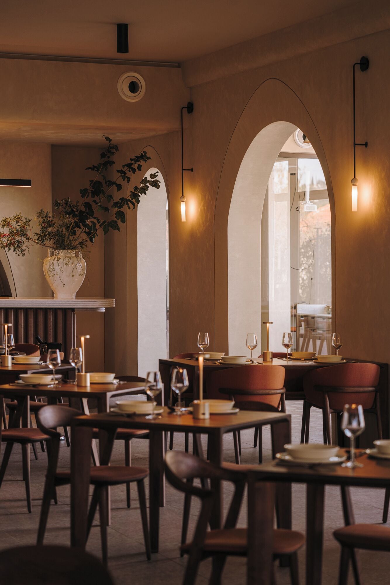 Interior de restaurante com mesas e cadeiras de madeira, e janelas em arco.