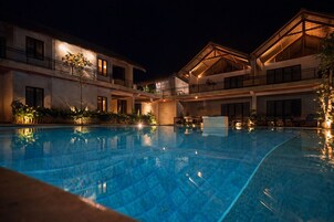 Vista noturna de um hotel com piscina, várias varandas e iluminação externa.