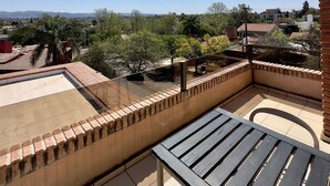 Um terraço no telhado com vista para uma área residencial, incluindo árvores e edifícios.