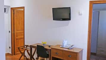 Quarto com escrivaninha de madeira, uma cadeira, televisão na parede e uma porta.