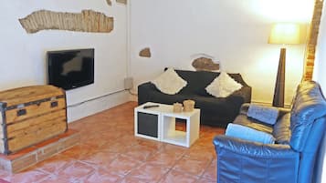Uma sala de estar com televisão, sofá, poltrona de couro, luminária e uma mesinha com controle remoto.