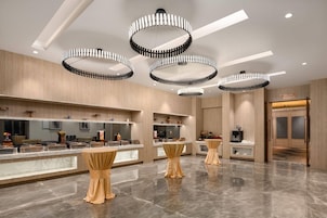Um hall de hotel moderno com balcões de mármore, mesas com detalhes dourados e lustres circulares.