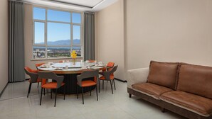 Uma sala de estar moderna com uma mesa de jantar redonda, cadeiras laranja, um sofá de couro marrom e uma janela grande com vista para a cidade.