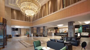 Um hall amplo com um lustre imponente, assentos confortáveis, área de recepção e bar.