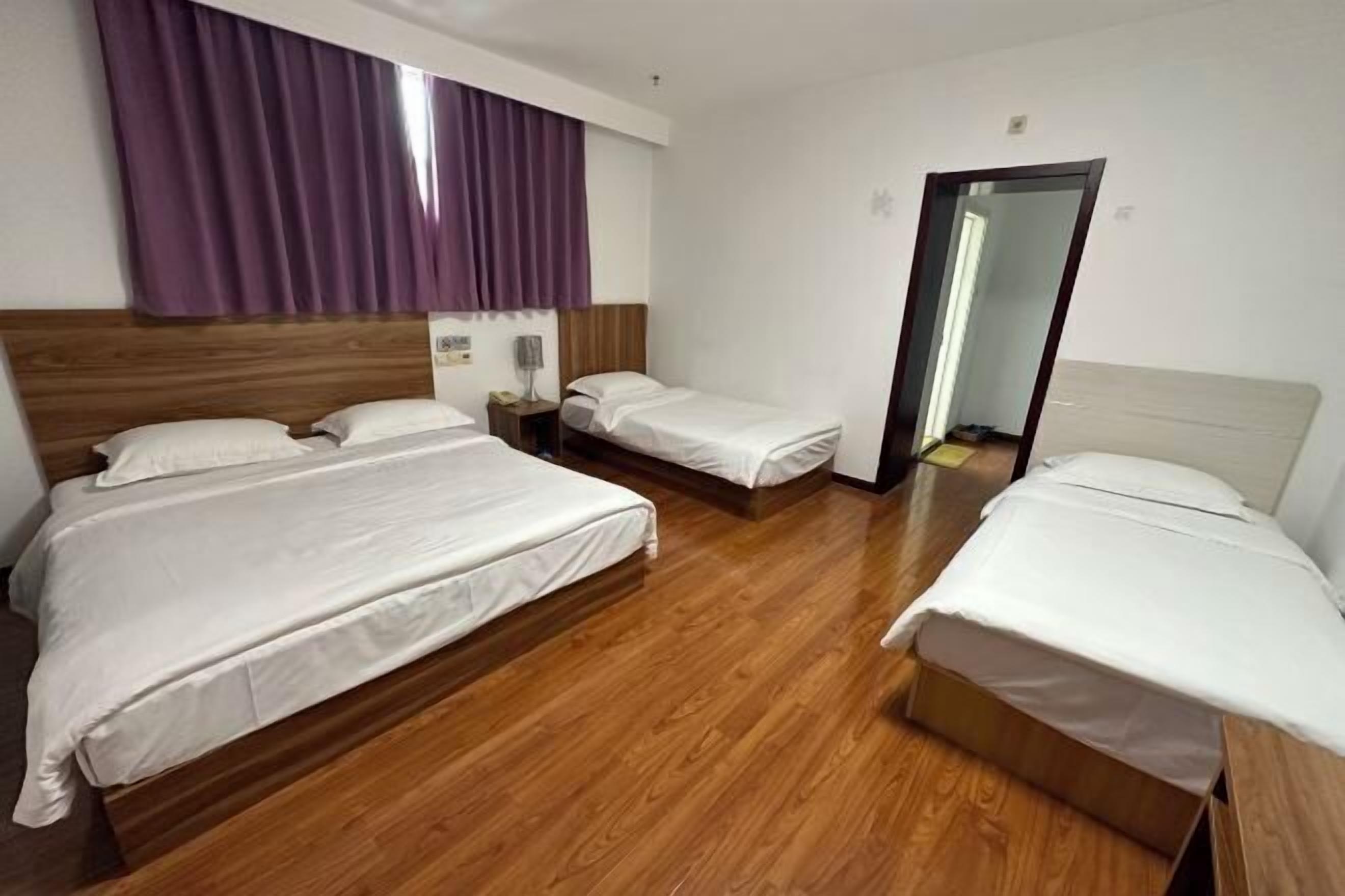 Quarto de hotel com duas camas, piso de madeira, espelho e porta.