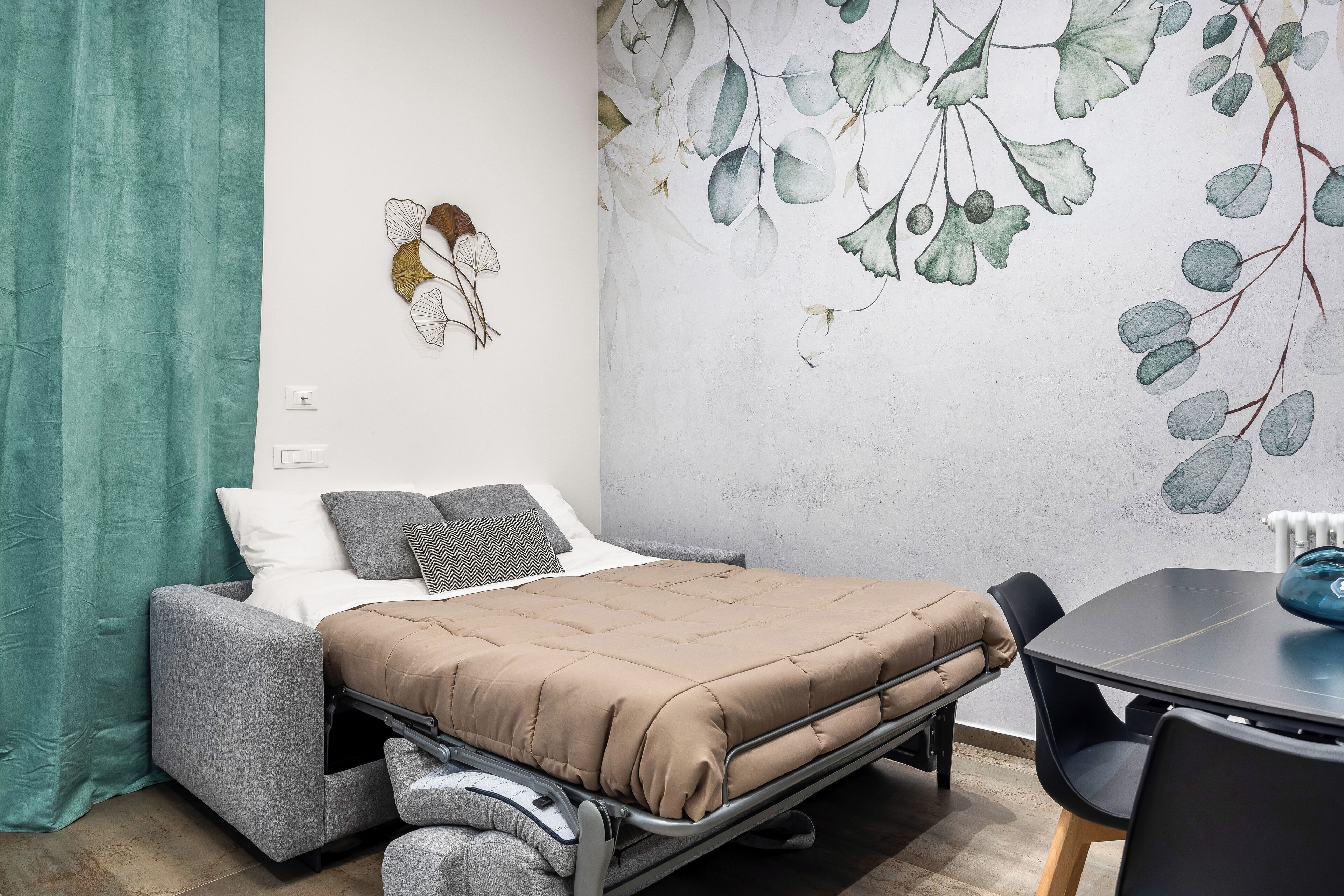 Quarto pequeno com cama, mesa e cadeira.