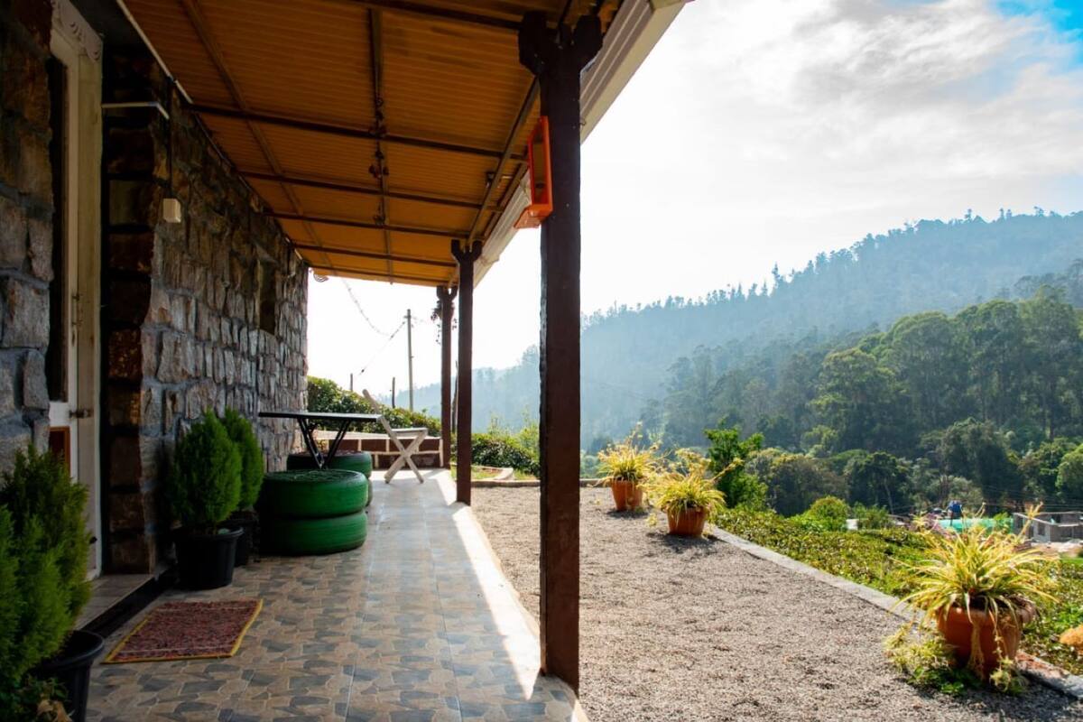 Um espaço coberto ao ar livre com parede de pedra, mesa, cadeiras e plantas em vasos.