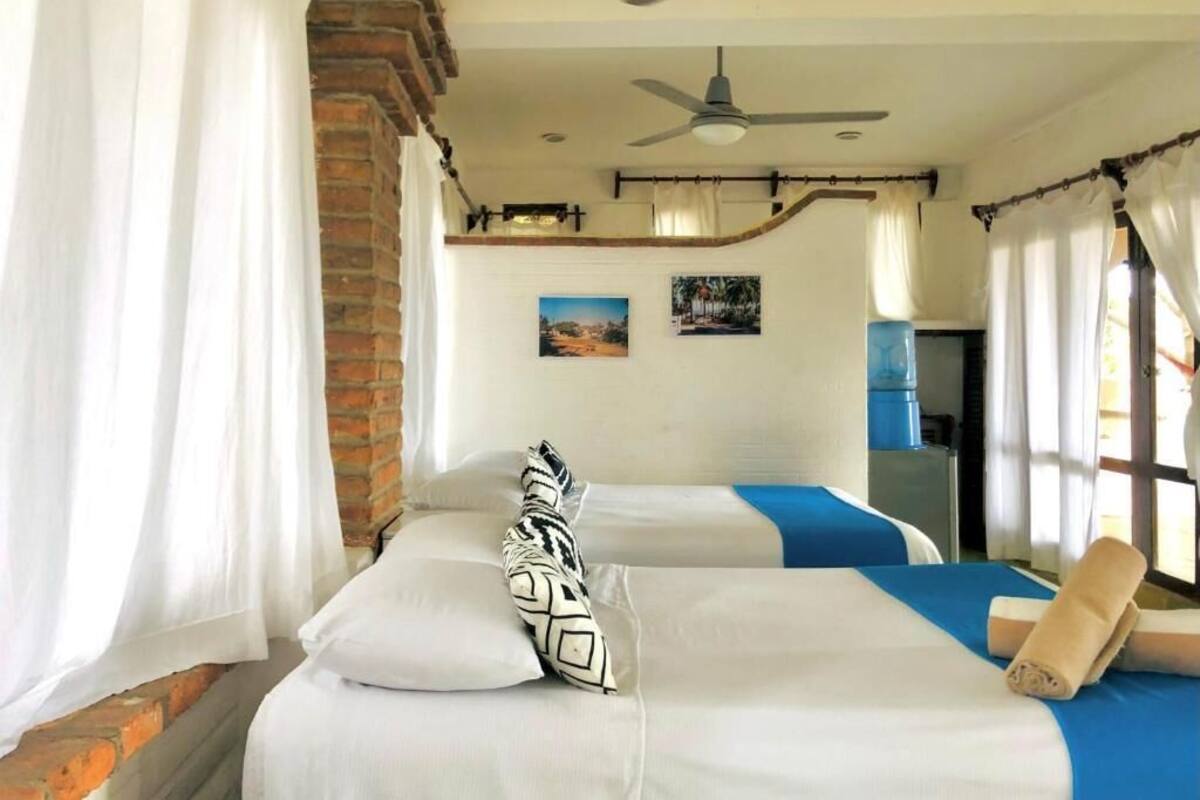 Quarto de hotel com duas camas, um ventilador de teto e uma parede de tijolos.