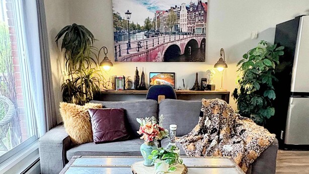 Uma sala de estar com uma mesa de centro em formato de mala antiga, um sofá e um quadro de uma ponte.