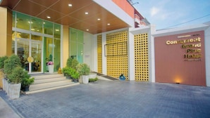 Entrada de hotel com design moderno, apresentando fachada de vidro e fachada de madeira, e um letreiro com a inscrição 'Convenient Grand Plus Hotel'.