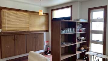 Quarto com armários de madeira, sofá, estante com copos e janela com persianas.