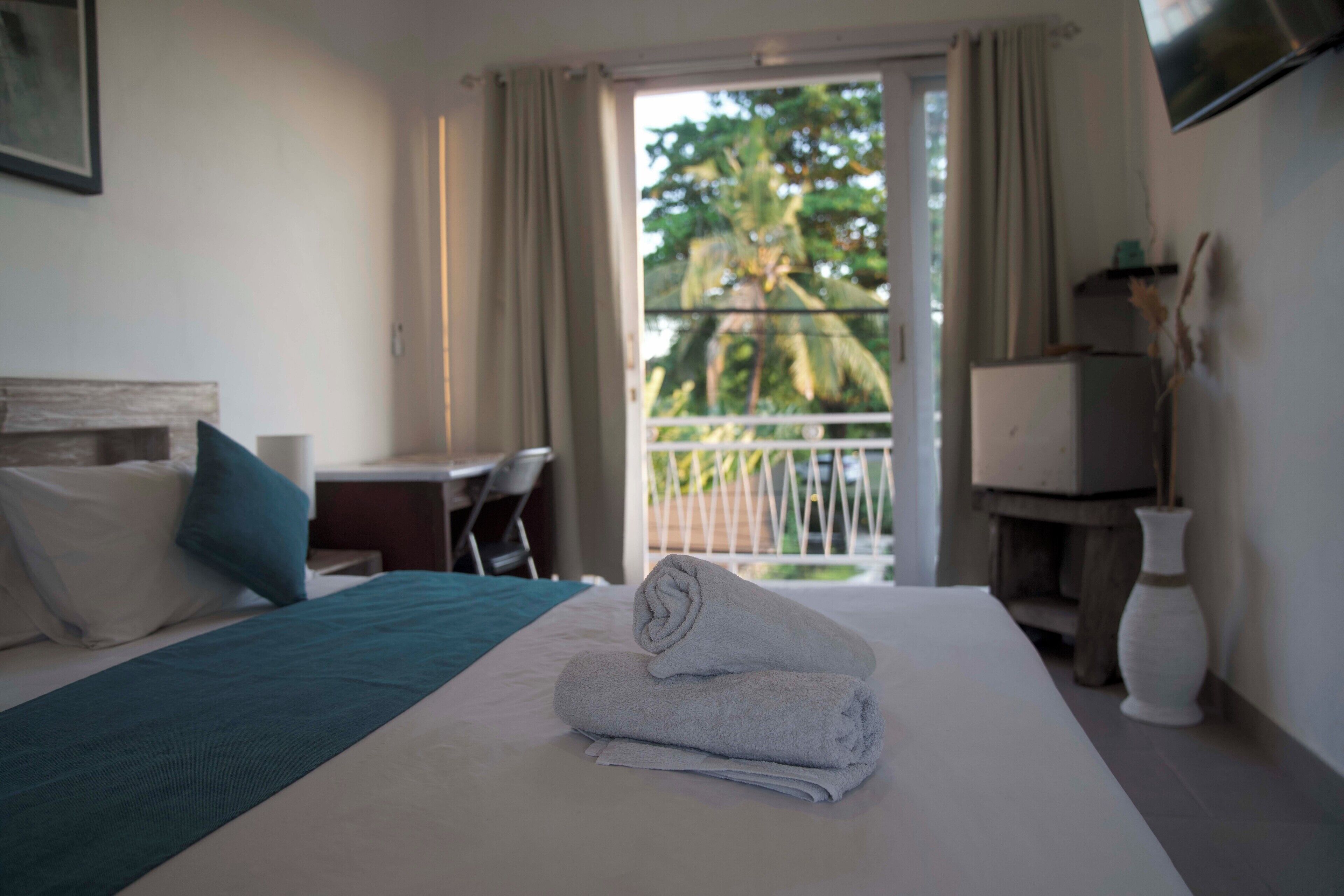 Quarto de hotel com cama, escrivaninha, televisão e vista para o exterior.