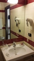 Casa de banho com lavatório branco, dois secadores de cabelo fixados na parede, espelho e porta-toalhas.