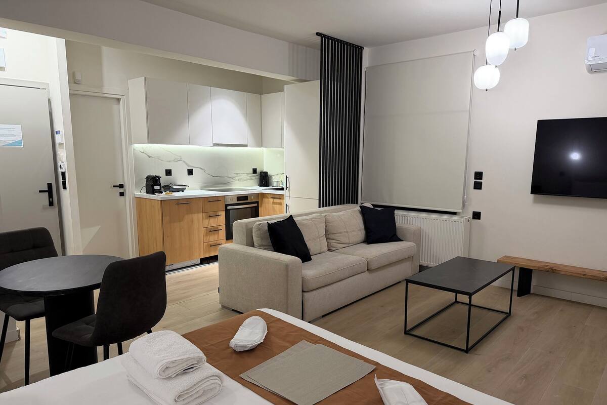 Quarto de hotel moderno com área de refeições, cozinha compacta e uma televisão grande.