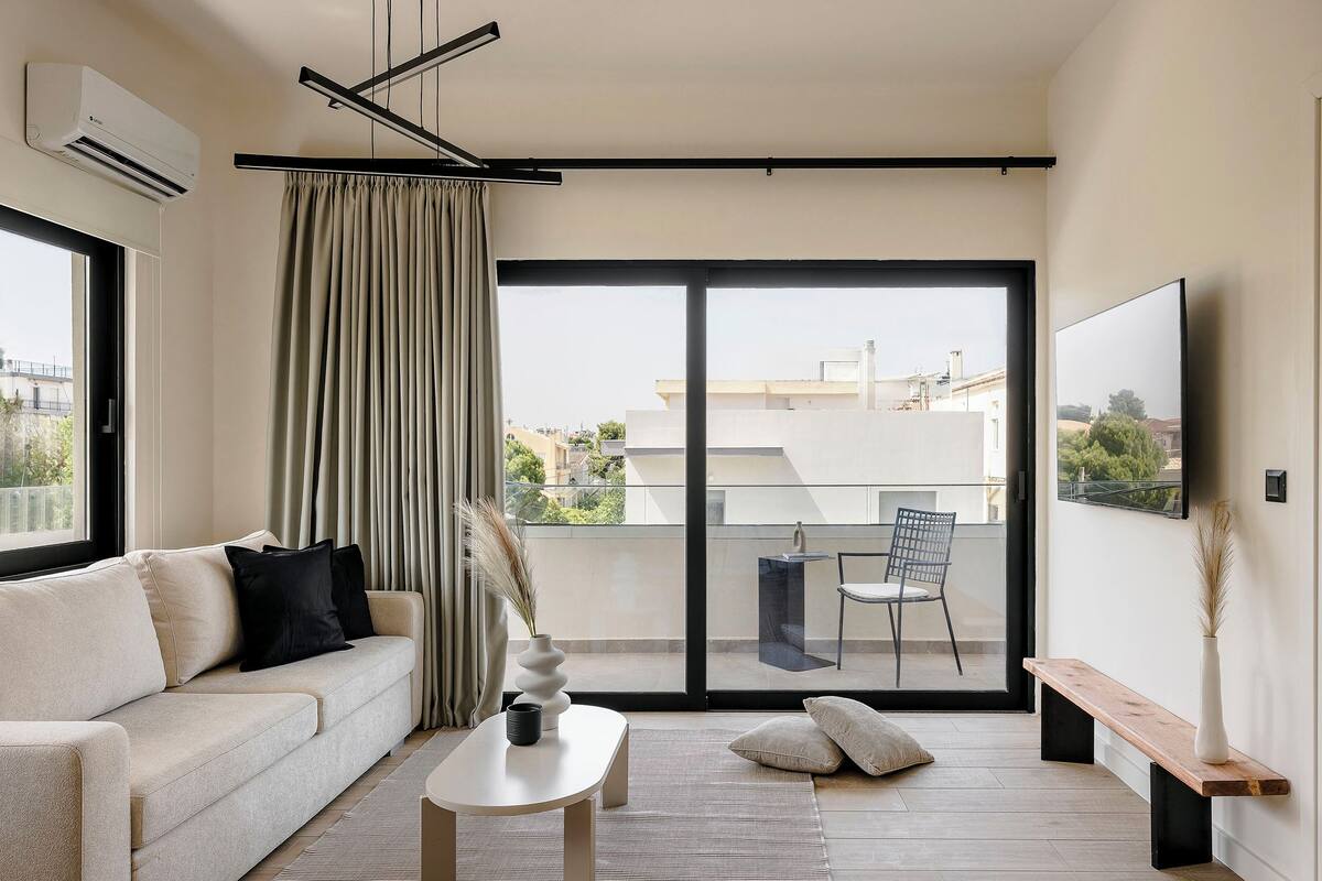 Uma sala de estar moderna com sofá, mesa de centro, um banco e uma varanda com cadeira.