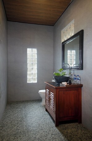 Casa de banho com toucador de madeira, um espelho grande e janela com padrão quadriculado.