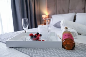 Uma bandeja com duas taças, uma tigela de frutas vermelhas e uma garrafa de vinho rosé sobre uma cama.