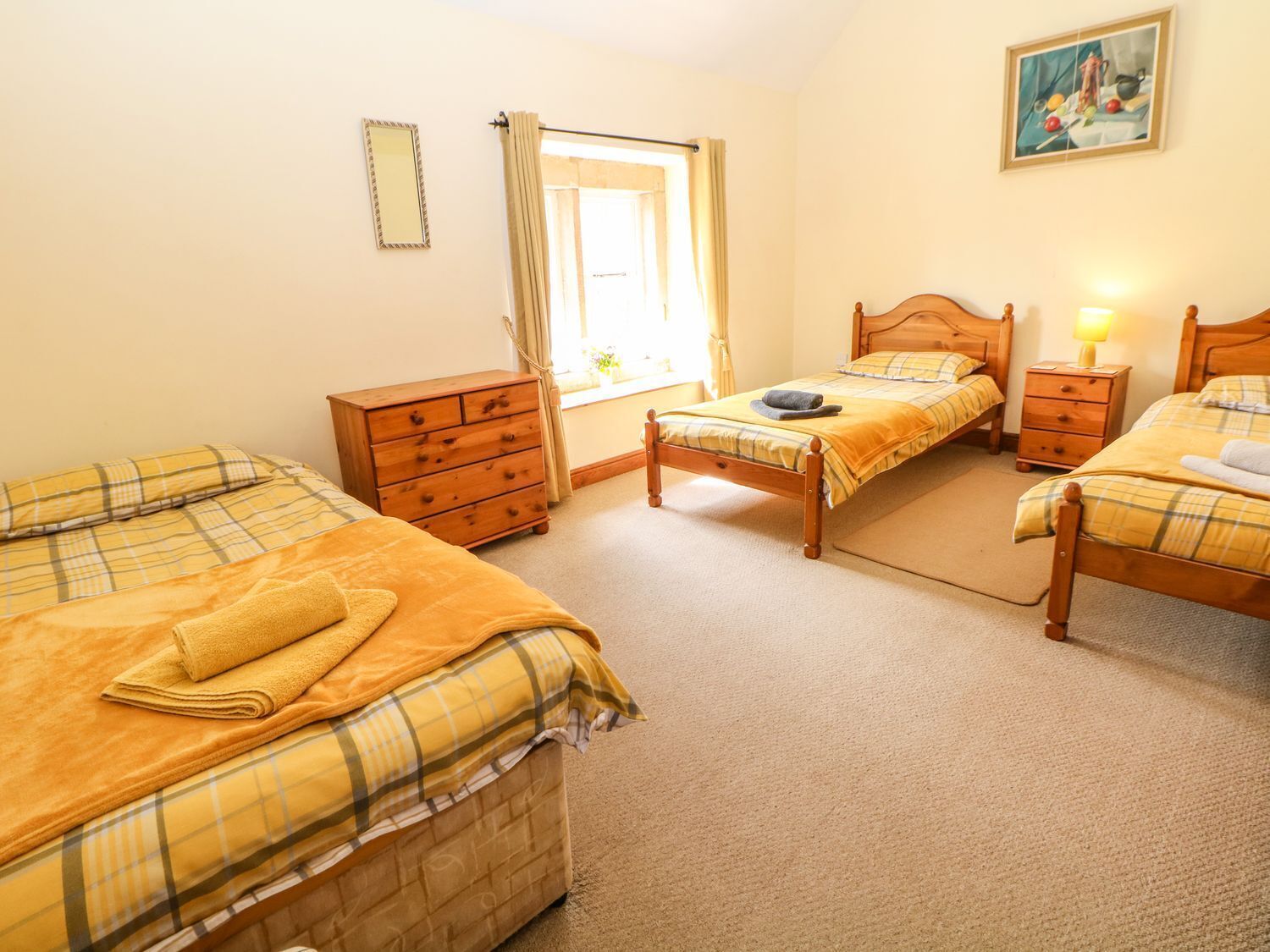 Quarto com duas camas, uma cômoda de madeira, mesa de cabeceira, janela com cortinas e um quadro na parede.