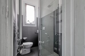 Casa de banho moderna com sanita, cabine de duche em vidro e janela que proporciona luz natural.