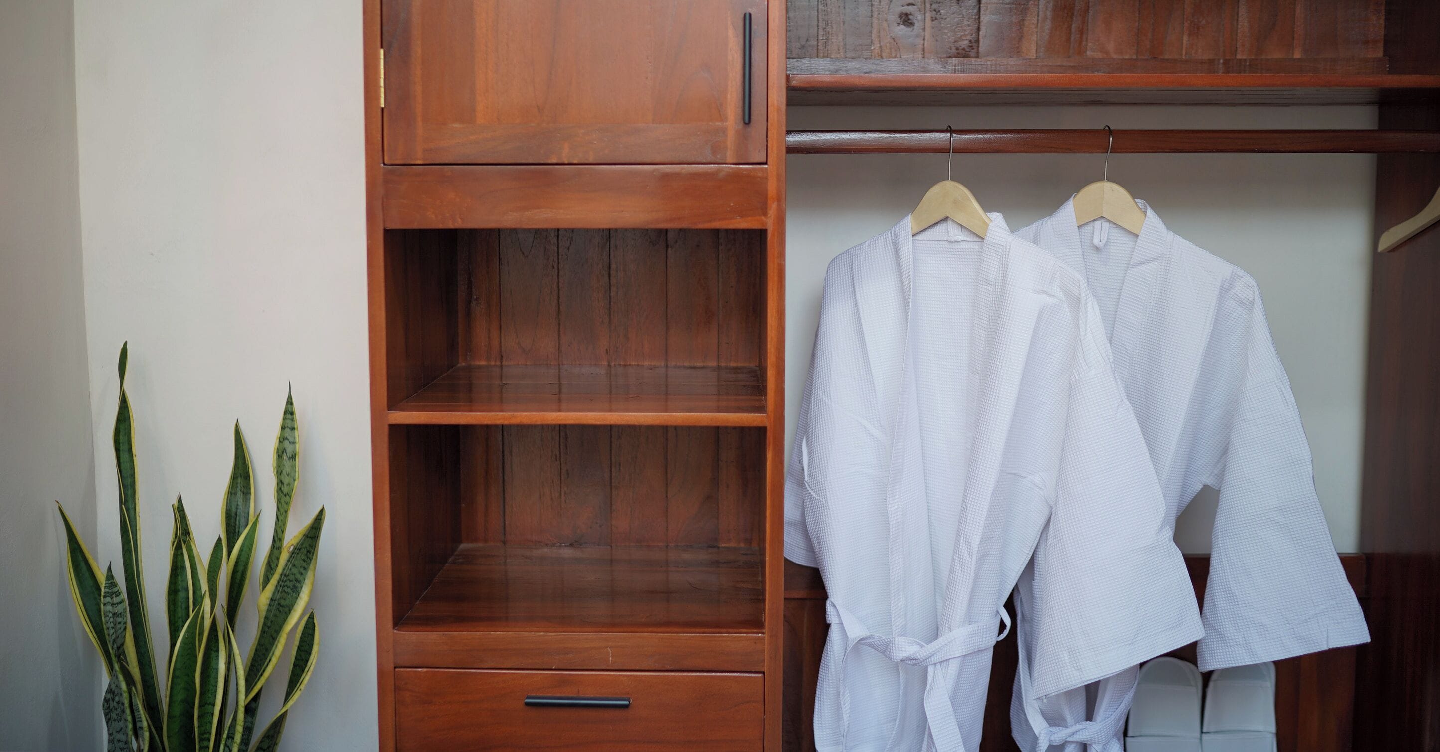 Um guarda-roupa de madeira com dois robes brancos pendurados em um cabide de madeira.