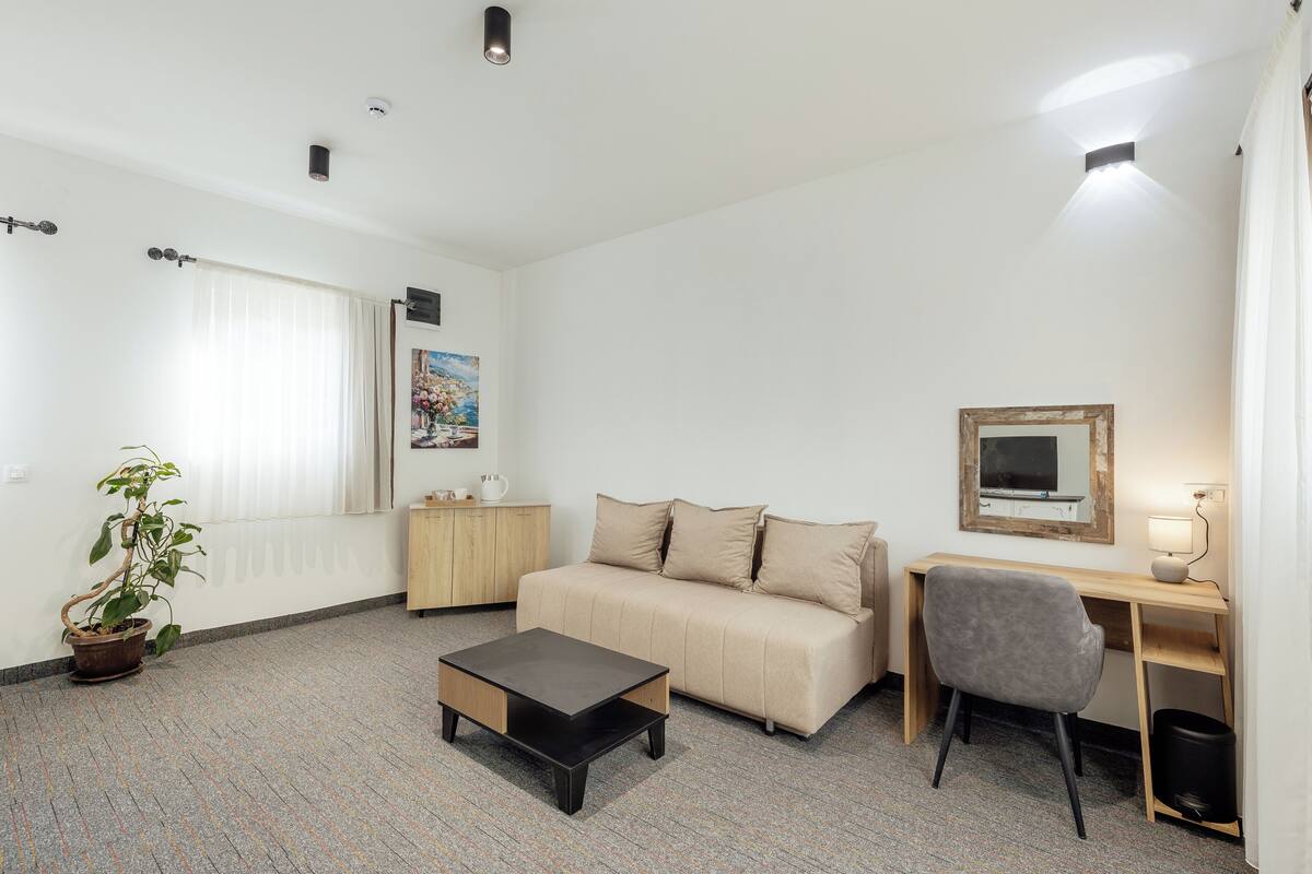 Quarto moderno com sofá, escrivaninha, cadeira, mesinha, planta em vaso, radiador, quadro na parede e luminária de teto.