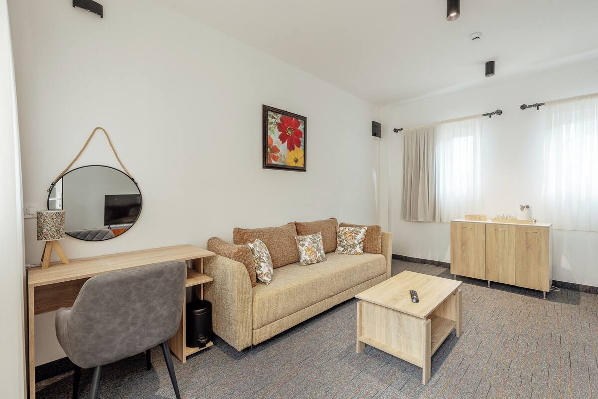 Uma sala de estar moderna com um sofá, uma escrivaninha, uma cadeira, uma mesa de centro, um armário e um espelho grande.