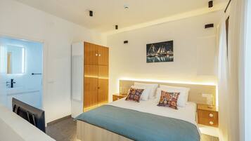 Quarto de hotel moderno com uma cama grande, um guarda-roupa de madeira, uma mesa de cabeceira com abajur e um quadro na parede.