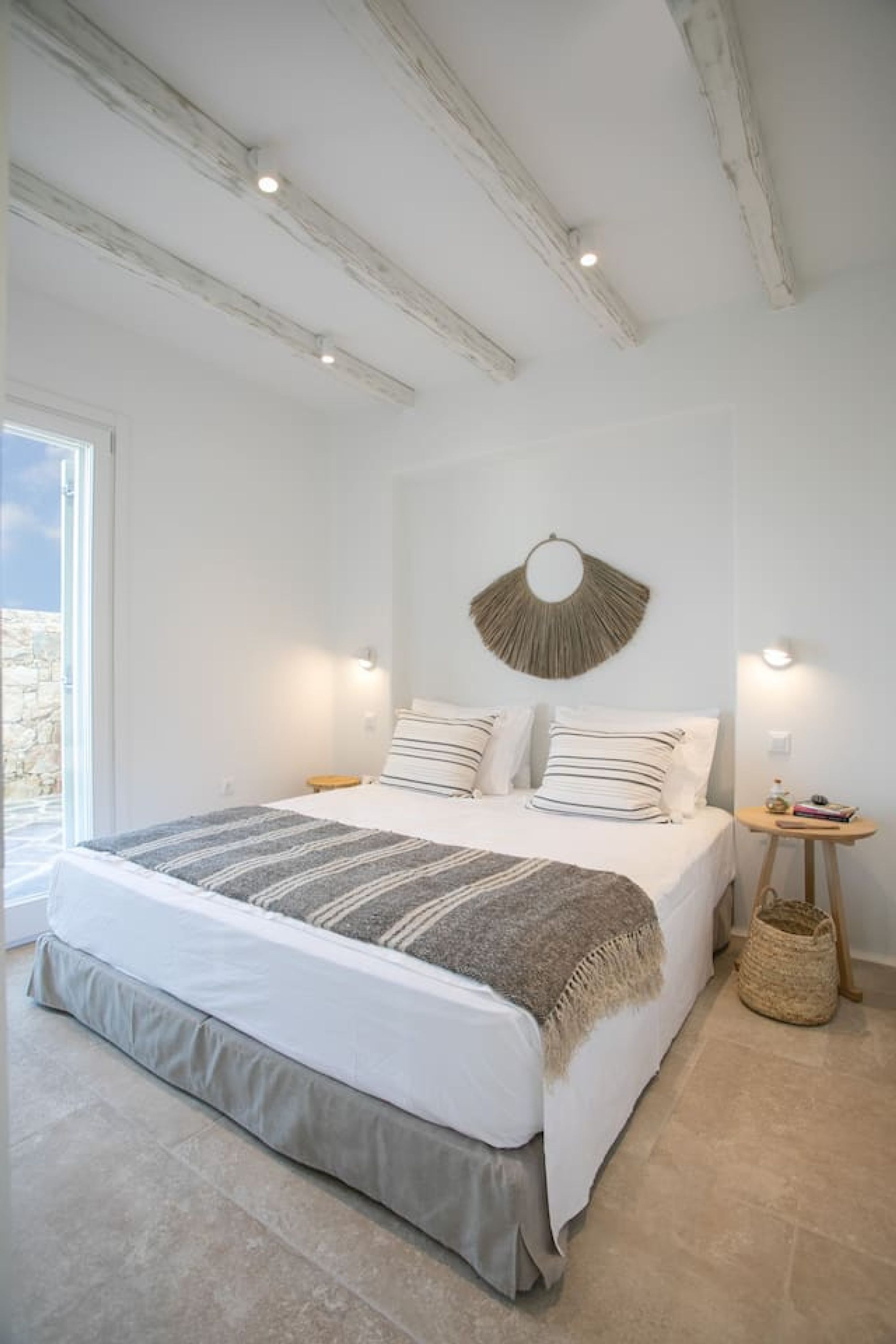 Quarto com cama grande, duas mesas de cabeceira, luminária na parede e vista para o exterior.