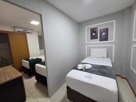 Quarto de hotel com cama, escrivaninha, cadeira, espelho e ar condicionado fixado na parede.