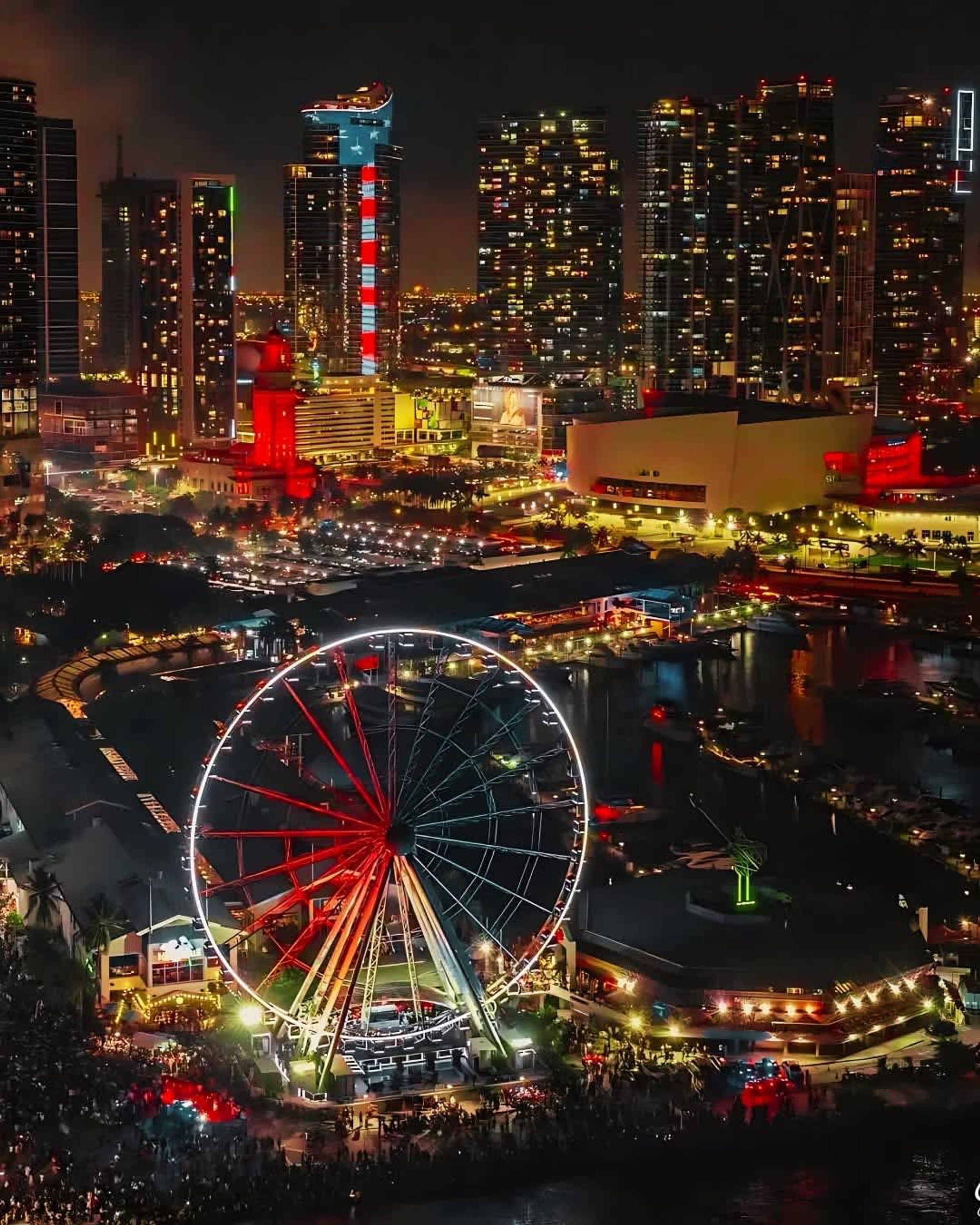 Paisagem urbana noturna com uma roda-gigante em destaque e edifícios altos.
